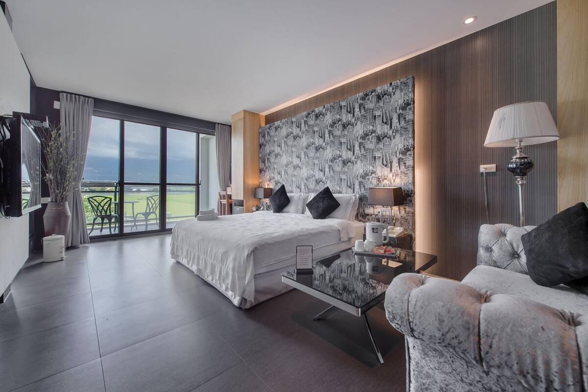 Quarto de hotel moderno com uma cama grande, um sofá, uma mesa de centro e um mural com vista para a cidade.