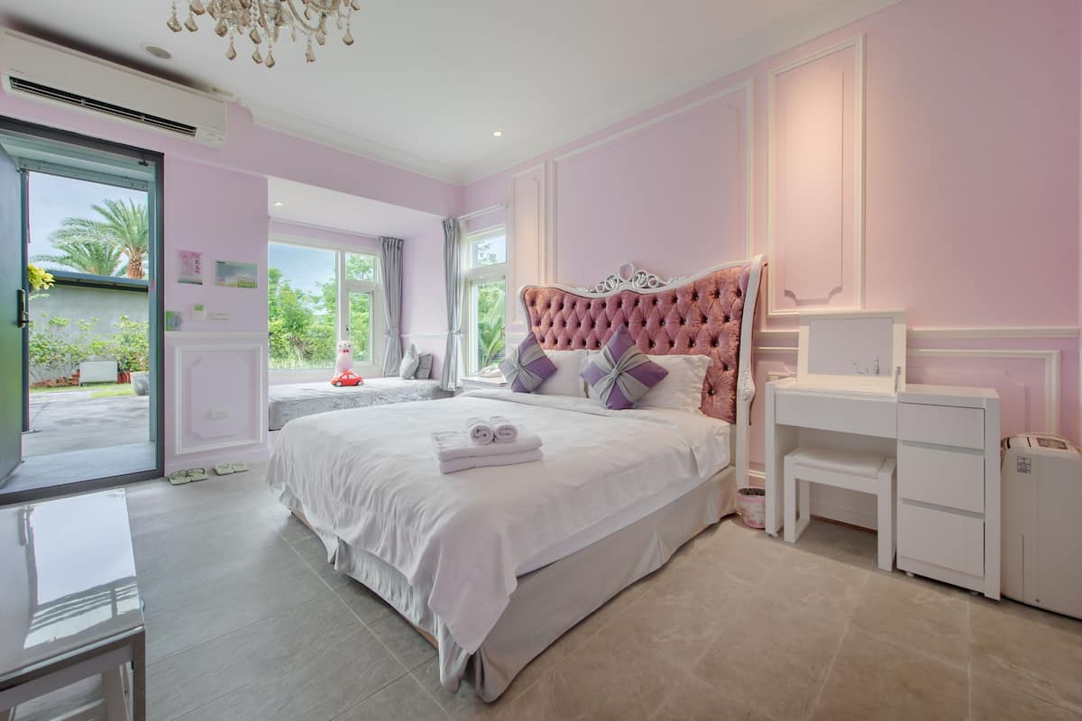 Quarto com cama grande, escrivaninha e cadeira. Janela com vista para área verde lá fora.