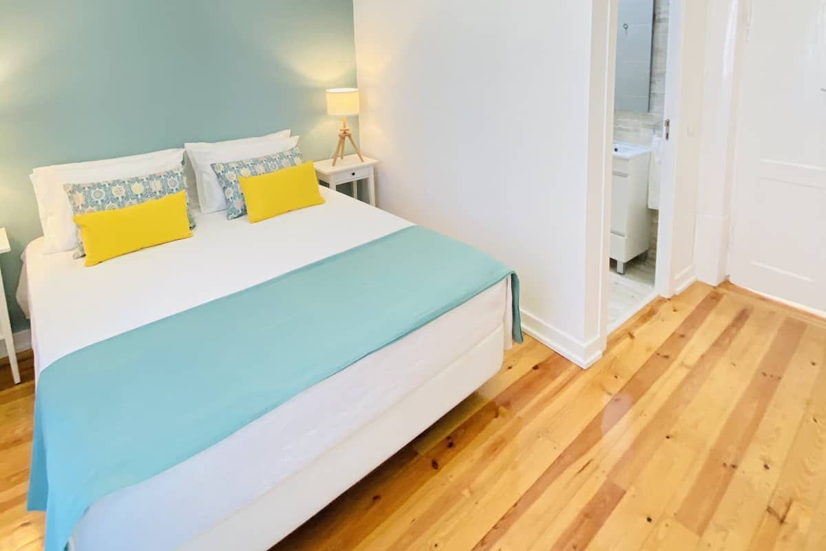 Quarto com cama, mesas de cabeceira, abajur e piso de madeira.