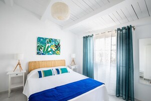 Quarto com cama, pintura, janela com cortinas e abajur em uma mesa de cabeceira.