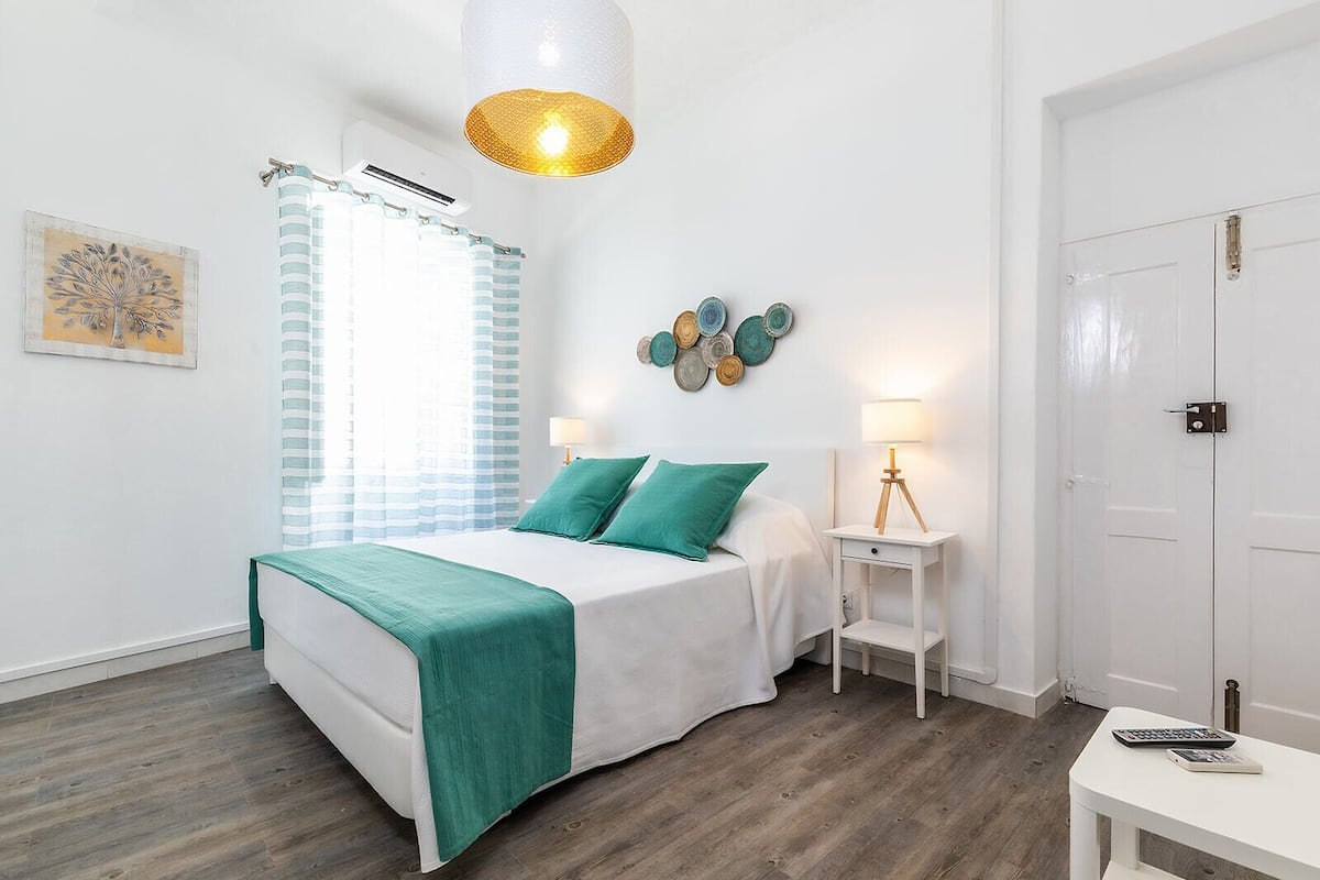 Quarto com cama, mesas de cabeceira, luminária, obra de arte na parede e uma porta.