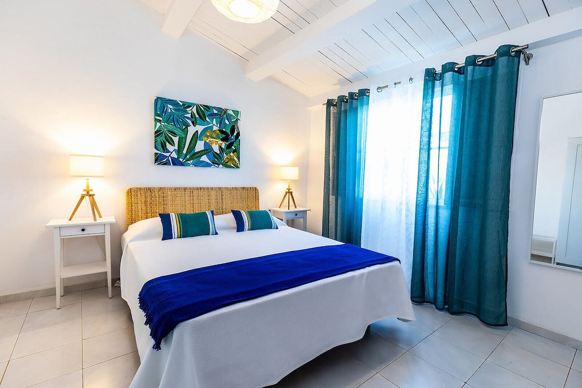 Um quarto moderno com uma cama grande, duas mesas de cabeceira com luminárias, uma cabeceira e um quadro na parede.