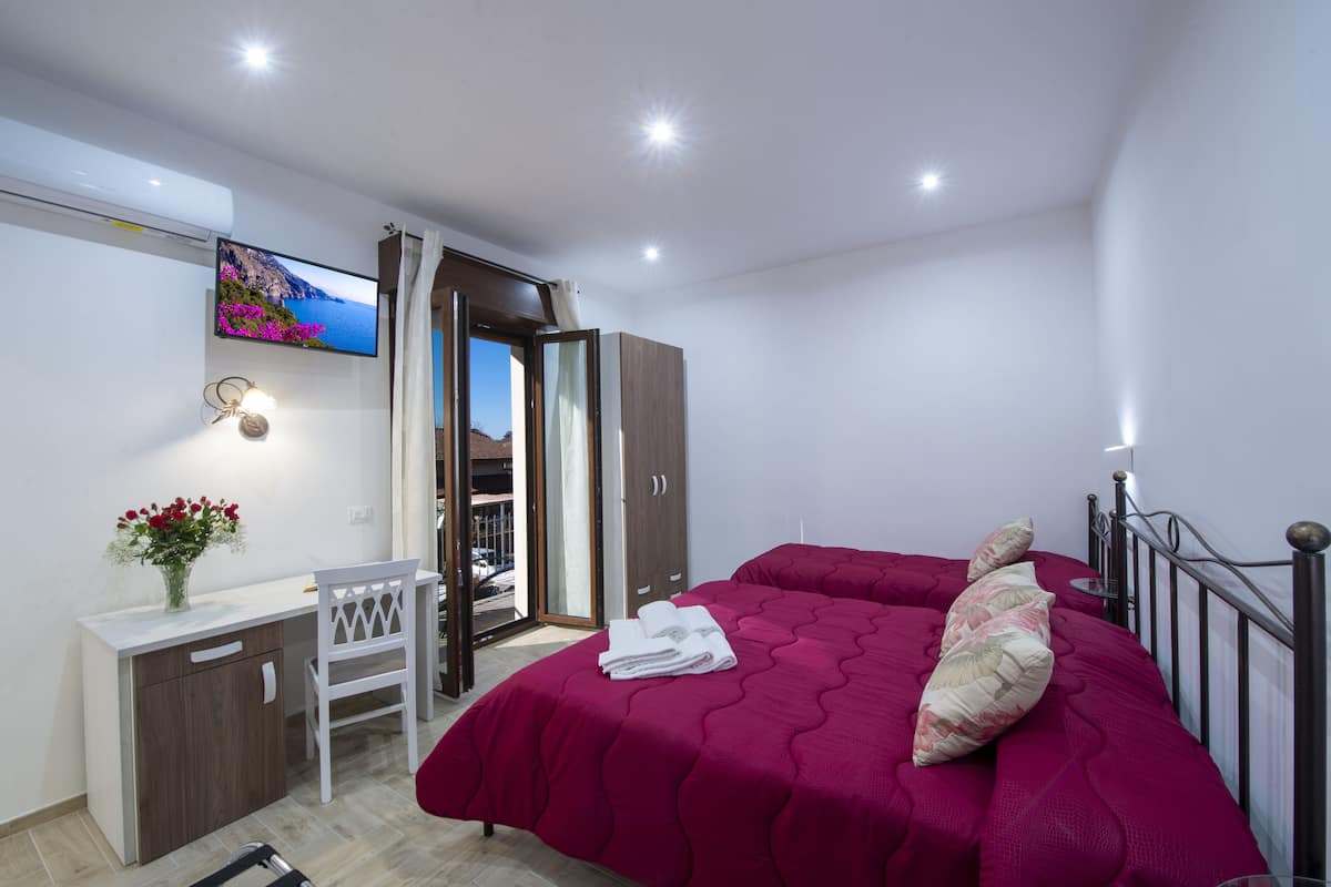 Quarto com cama, escrivaninha, cadeira, televisão e vista para o exterior.
