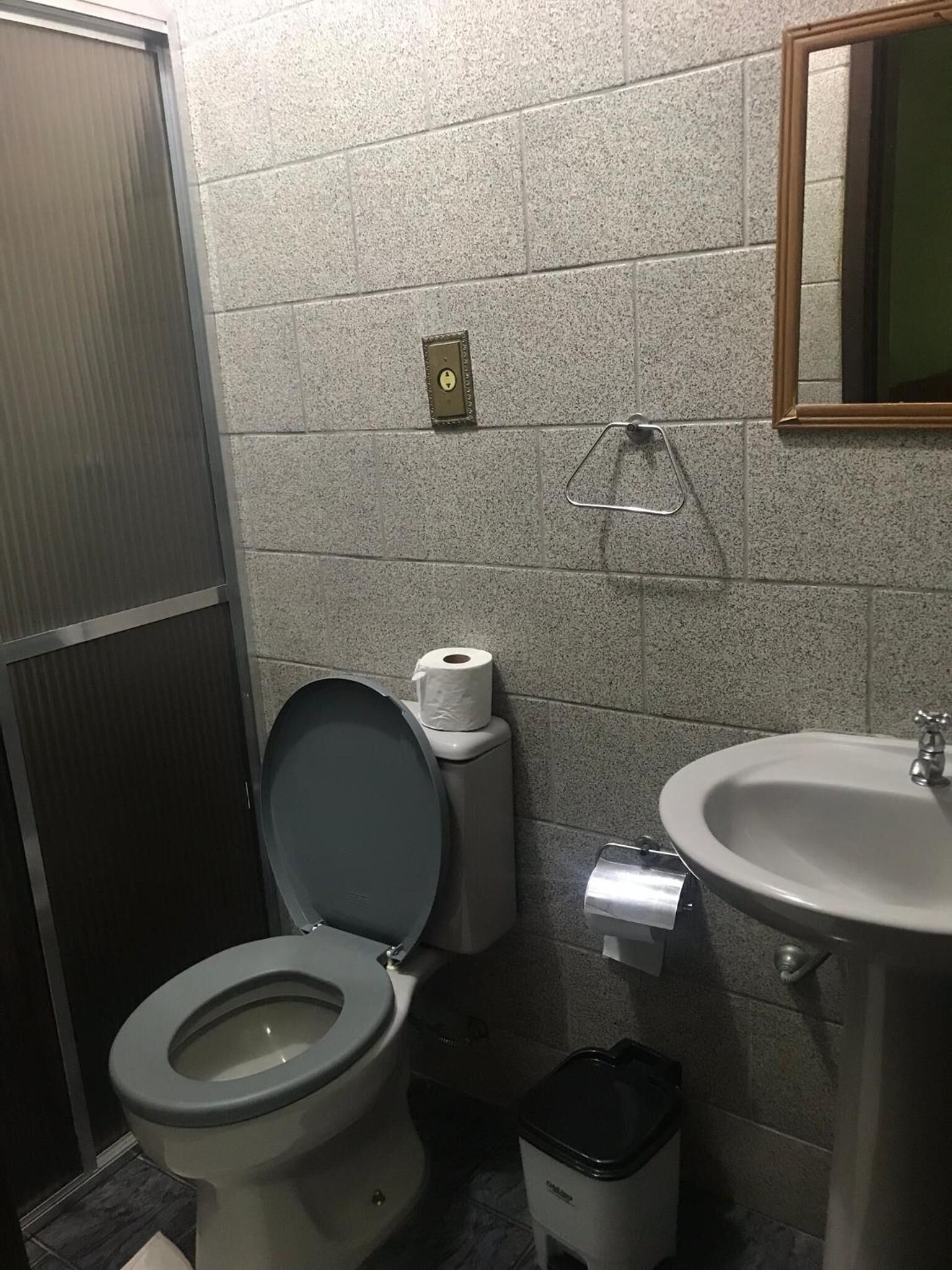 Casa de banho com sanita, lavatório e um contentor de lixo.