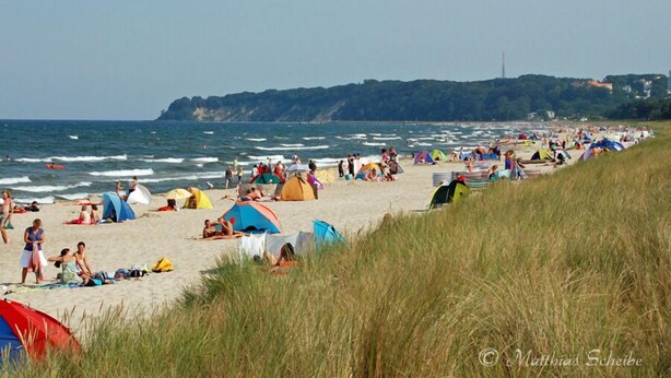 Praia lotada com tendas e pessoas.