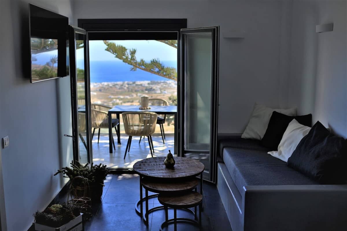 Uma varanda com sofá, mesa e cadeiras, oferecendo uma vista panorâmica do mar e da paisagem ao longe.