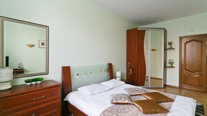 Quarto com cama, cómoda, espelho, guarda-roupa e uma porta.
