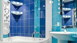Casa de banho com azulejos azuis, uma banheira branca, lavatório e espelho com iluminação.