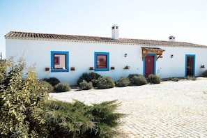 Um edifício branco com janelas e portas emolduradas em azul, um telhado ladrilhado e uma entrada com calçada de pedras.