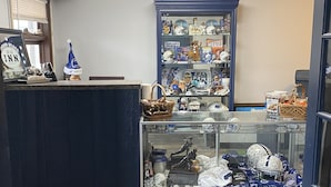 Uma área de recepção com balcão, uma vitrine de vidro repleta de itens de coleção esportiva e o logotipo emoldurado da Penn State na parede.
