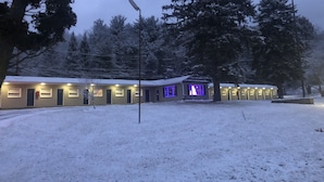 Um edifício coberto de neve com várias divisões, uma área central iluminada e árvores ao redor.