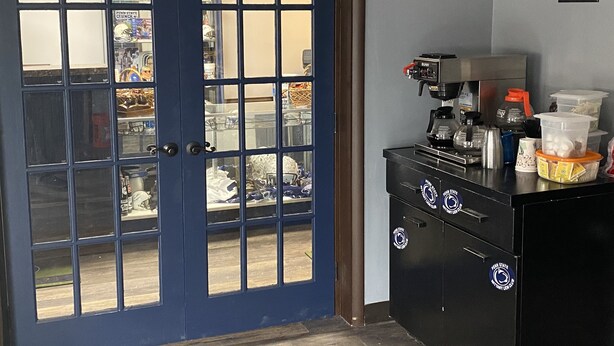 Um quarto com porta azul, uma máquina de café e uma estante com diversos objetos.