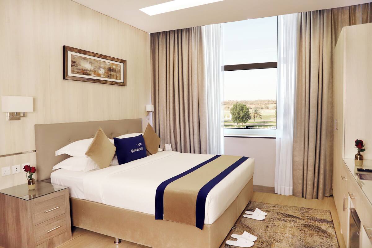 Quarto de hotel com uma cama grande, uma mesa de cabeceira, uma escrivaninha e vista para o exterior.