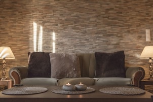 Uma sala de estar moderna com parede com padrão de pedra, sofá de couro com almofadas escuras e duas velas acesas sobre jogos americanos trançados.
