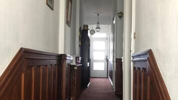 Um corredor com lambris de madeira, quadros nas paredes, um candelabro e uma porta ao fundo.