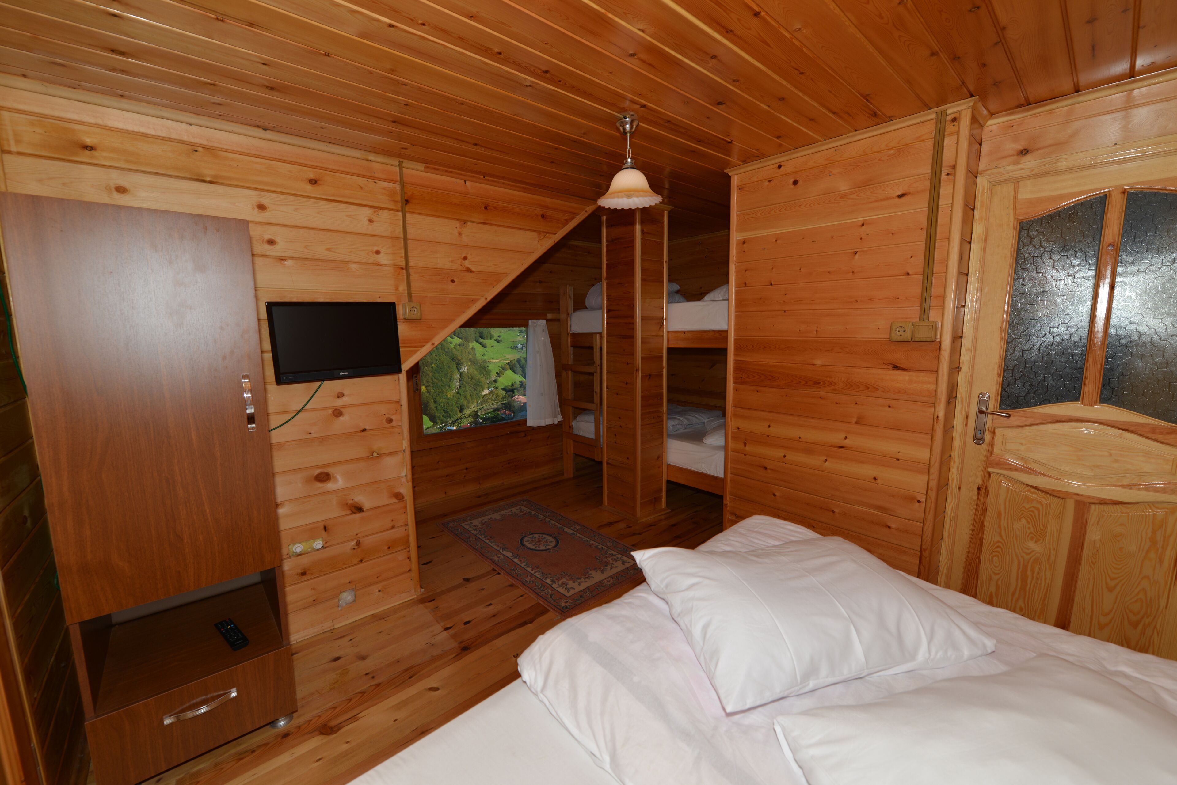 Quarto de cabana de madeira com beliches, televisão e uma pequena escrivaninha.
