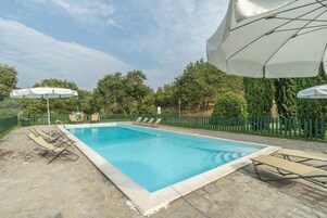 Piscina retangular com borda de pedra, rodeada por espreguiçadeiras e guarda-sóis.