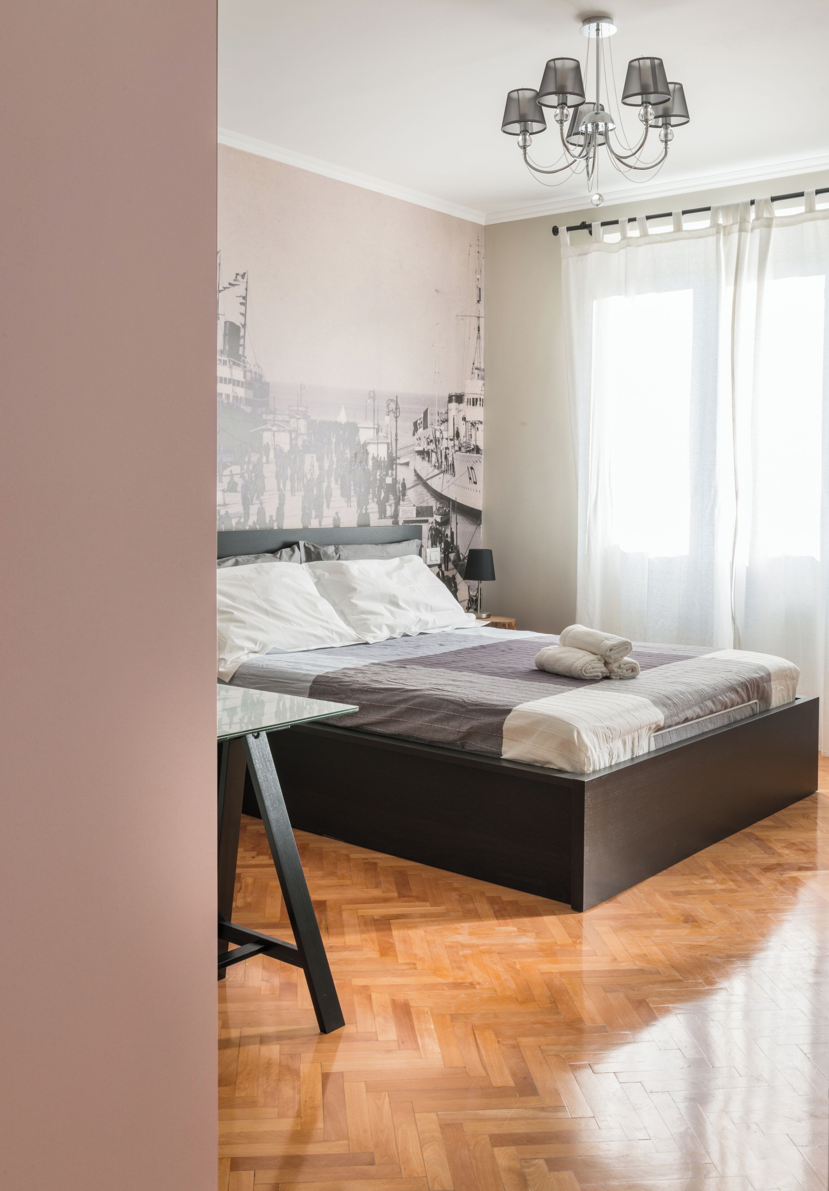 Um quarto moderno com cama, um candelabro e um mural da paisagem urbana na parede.