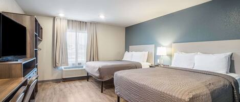 Quarto de hotel com duas camas, televisão, escrivaninha e janela com cortinas.