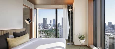 Quarto de hotel moderno com uma cama grande, vista para a cidade e um vaso de planta.
