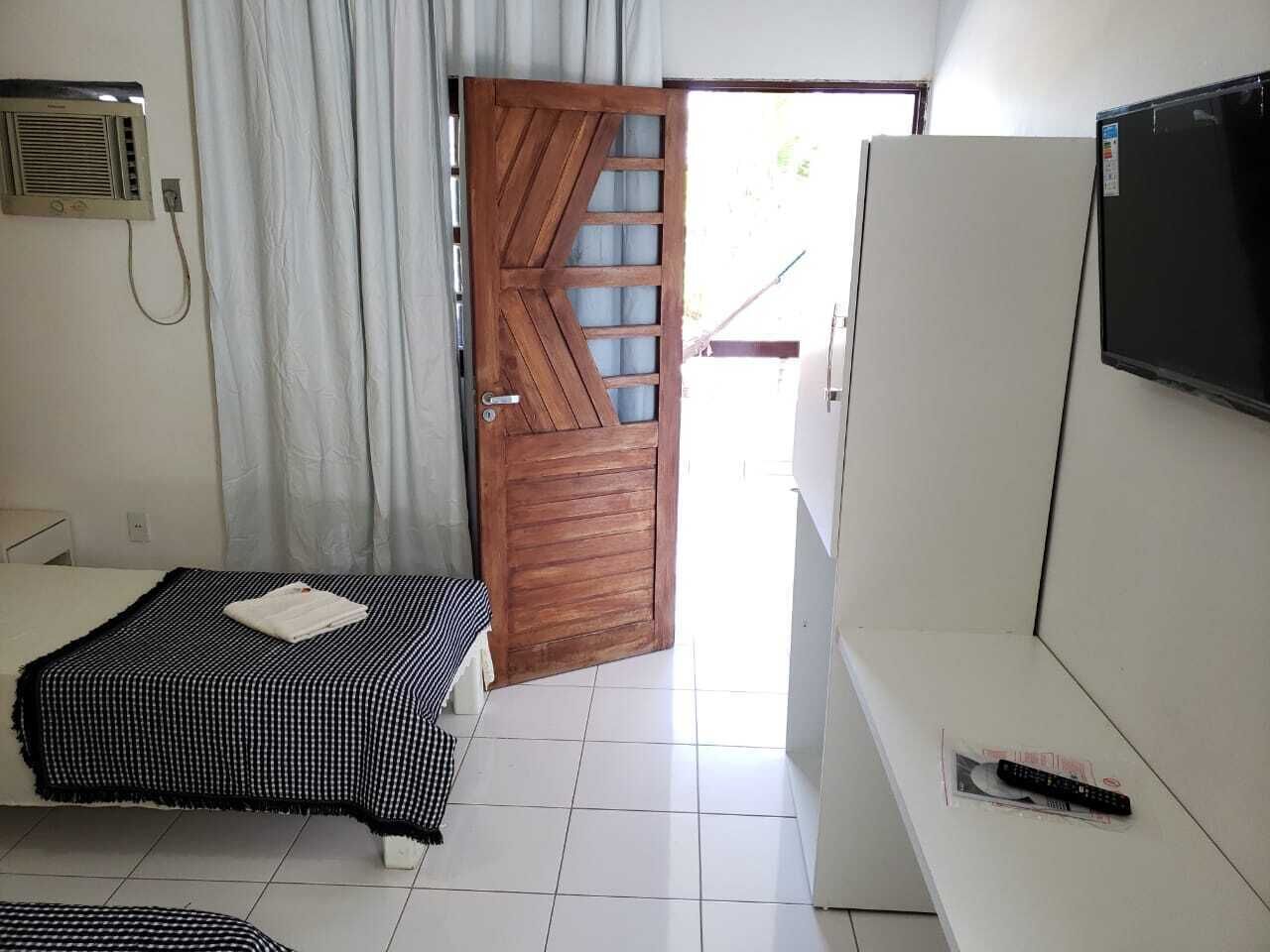 Um quarto com uma cama, uma porta de madeira, uma televisão e um controle remoto sobre uma mesa.