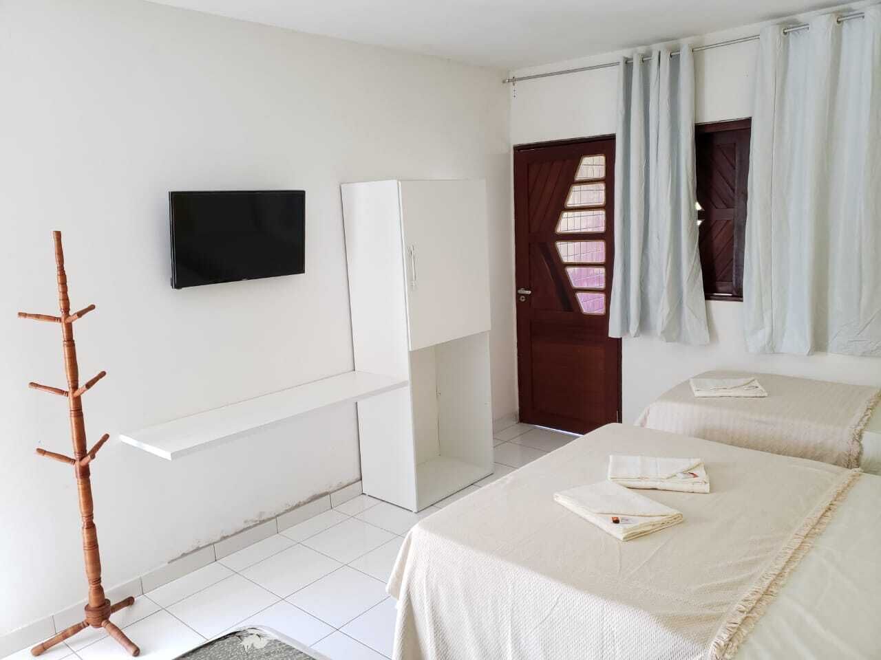 Quarto com duas camas, televisão, guarda-roupa e cabideiro.