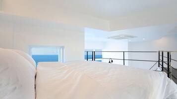 Quarto moderno com uma cama grande, varanda com guarda-corpo e vista para o mar.