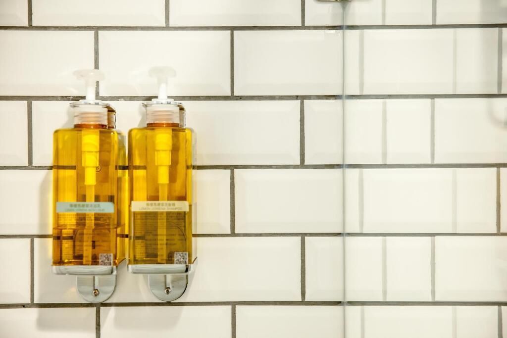 Dois dispensadores de álcool em gel amarelos fixados numa parede com azulejos brancos.