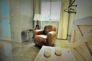 Quarto com poltrona de couro, uma mesinha redonda com abajur e duas xícaras sobre uma mesa de madeira.