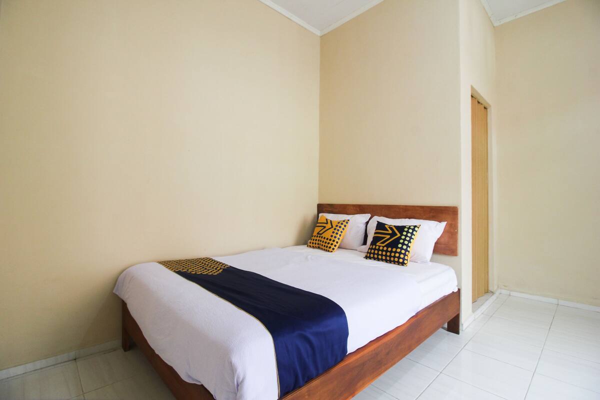 Uma cama bem arrumada com estrutura de madeira, roupa de cama branca e almofadas decorativas.