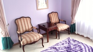Um quarto com duas poltronas, uma pequena mesa de madeira e um tapete roxo.