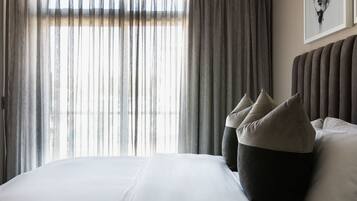 Quarto de hotel com uma cama grande, cortinas cinzentas e cabeceira com almofada.