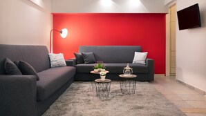 Uma sala de estar moderna com um sofá cinzento, uma parede de destaque vermelha e uma televisão de tela plana na parede.