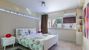 Quarto com cama, mesa de cabeceira, janela com cortinas e ar condicionado fixado na parede.
