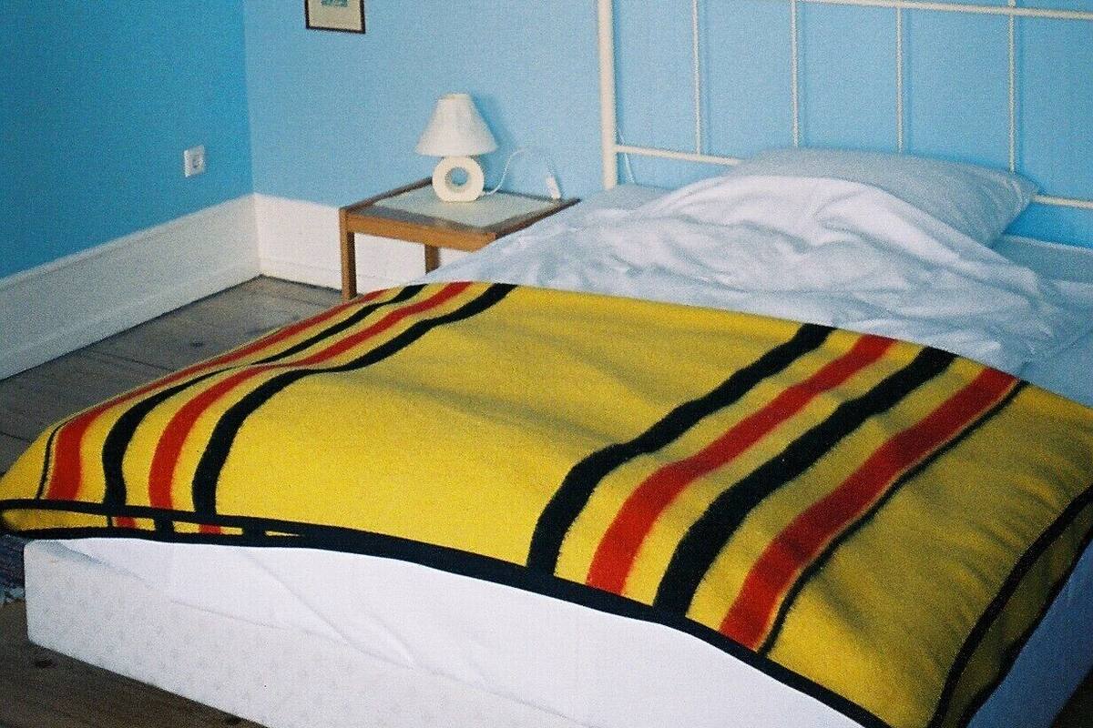 Quarto com uma cama de solteiro, mesa de cabeceira com luminária e quadro na parede.