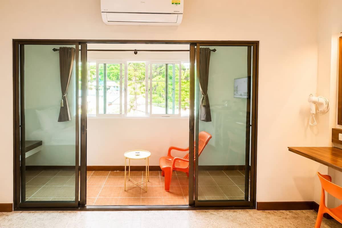 Quarto com porta de vidro deslizante para uma varanda, uma pequena mesa redonda, uma cadeira laranja e uma escrivaninha de madeira.