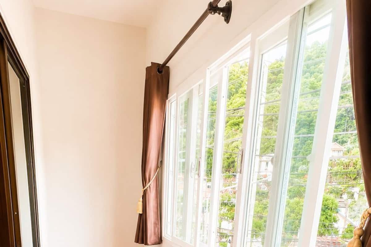 Quarto com um banco, uma mesa e uma janela com cortinas.