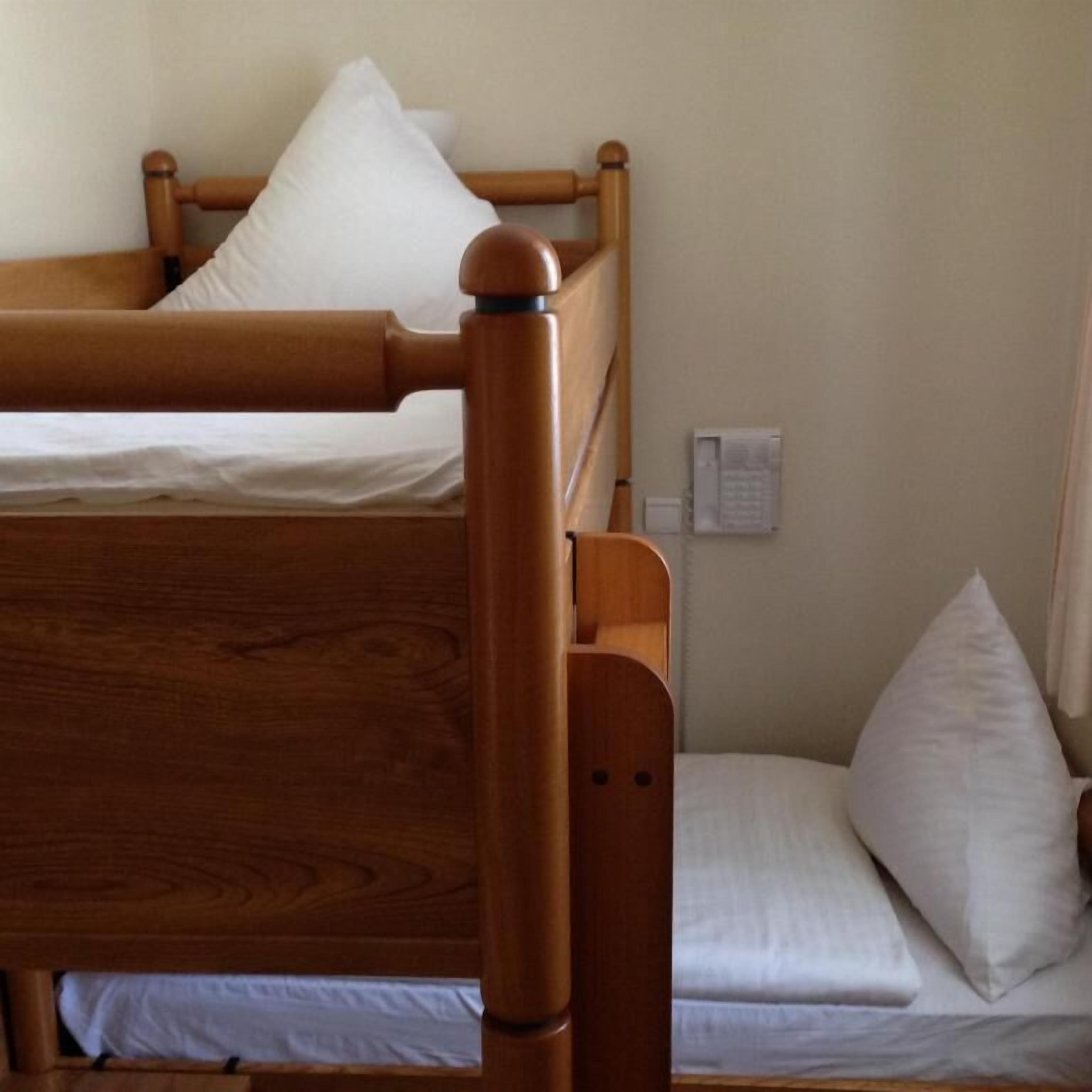 Uma cama de madeira com roupa de cama branca e um telefone ao lado.