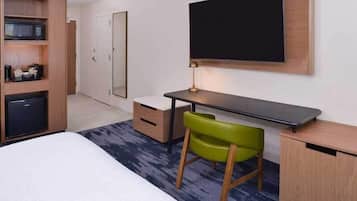 Quarto de hotel com cama, secretária, cadeira, televisão e guarda-roupa.