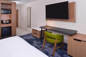 Quarto de hotel com cama, secretária, cadeira, televisão e guarda-roupa.