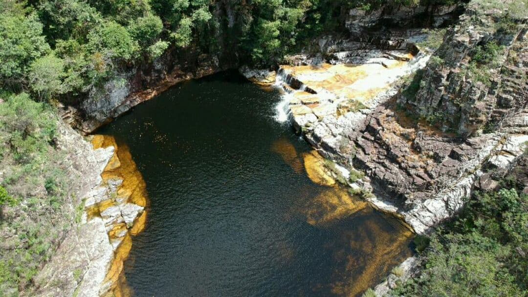 Uma massa de água natural rodeada por terreno rochoso e vegetação densa.