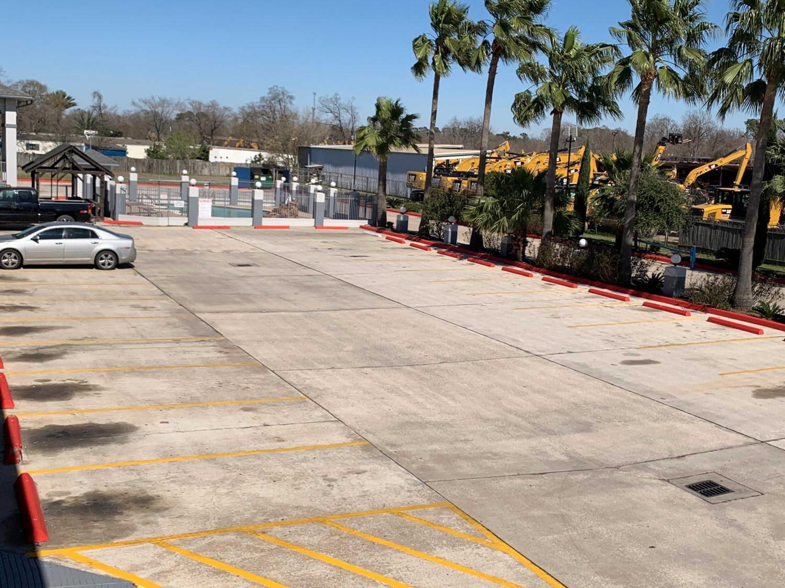 Um estacionamento com vagas demarcadas, um carro e equipamentos de construção ao fundo.