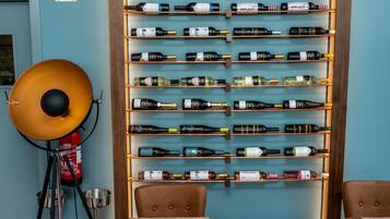 Interior de restaurante com uma parede de garrafas de vinho, mesas e cadeiras de madeira.