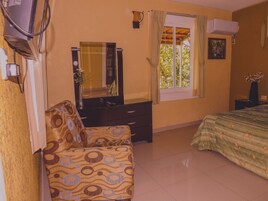Quarto com cama, cômoda, espelho, janela com cortinas e ar-condicionado fixado na parede.
