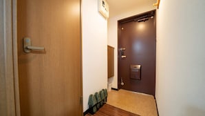 Um corredor com uma porta de madeira à esquerda, uma porta escura à direita e um sapateiro encostado na parede.