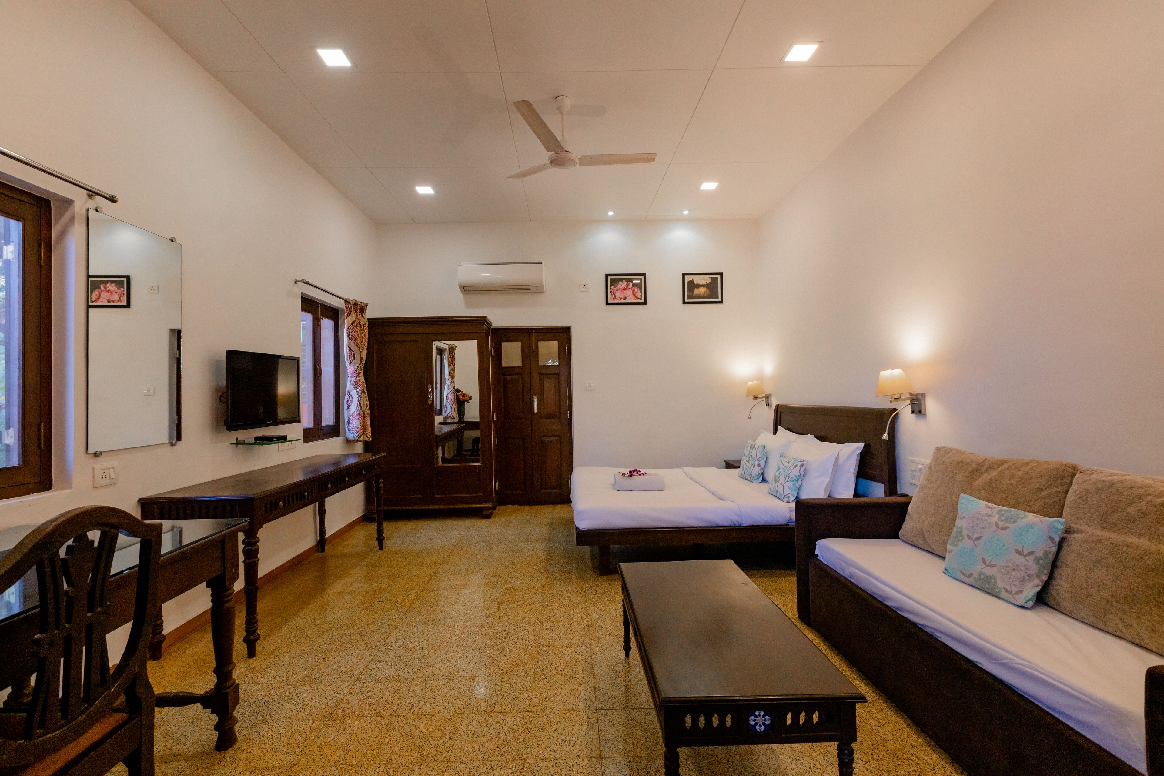 Quarto de hotel com cama, sofá, escrivaninha, cadeira e televisão.