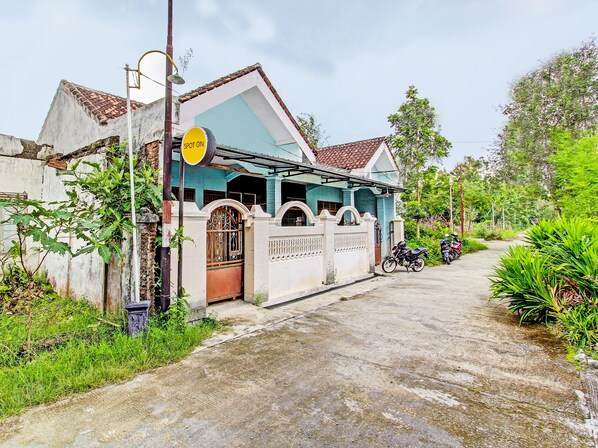 Uma casa com portão fechado, uma motocicleta estacionada na frente e uma rua arborizada.