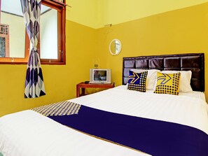 Quarto com cama, televisão sobremesa e janela com cortinas.
