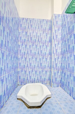Casa de banho com sanita squat branca, paredes em azulejo e chão estampado.