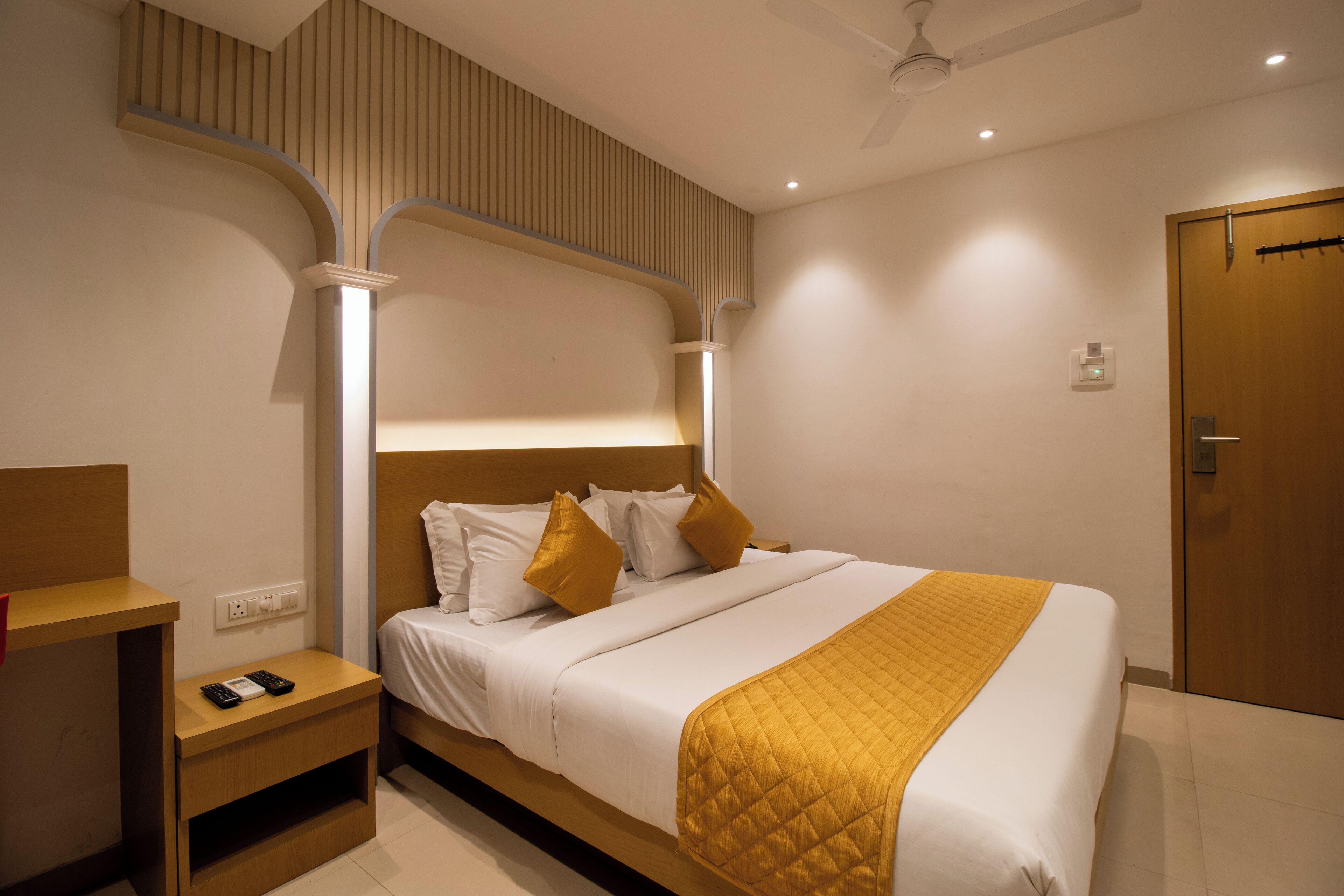 Quarto de hotel com cama, mesa de cabeceira e cabeceira de madeira.